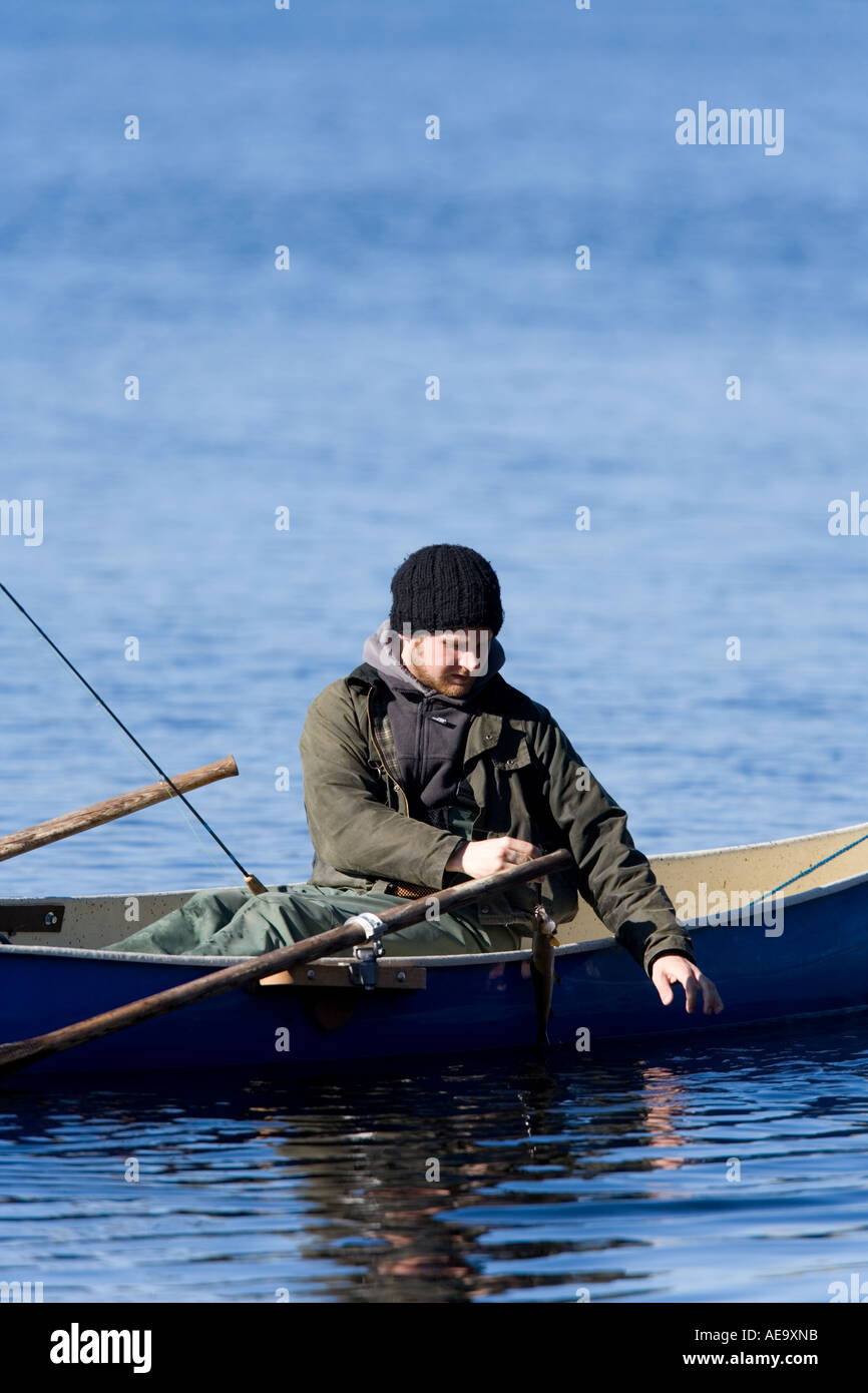 A man, fly-fishing from a blue canoe at early Spring, is just releasing ...