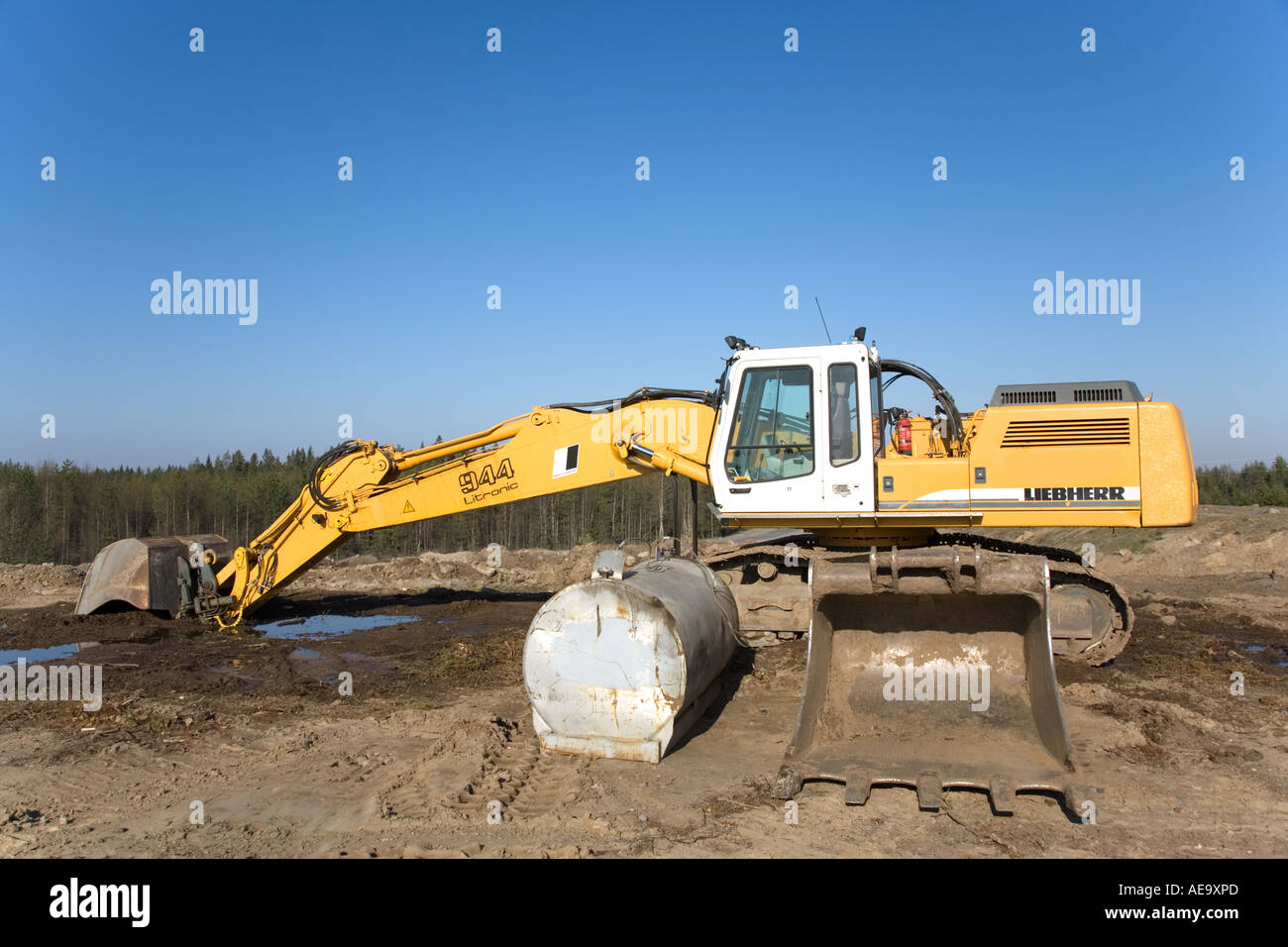 Yellow Liebherr digger, fuel tank and detached scoop against blue sky ...
