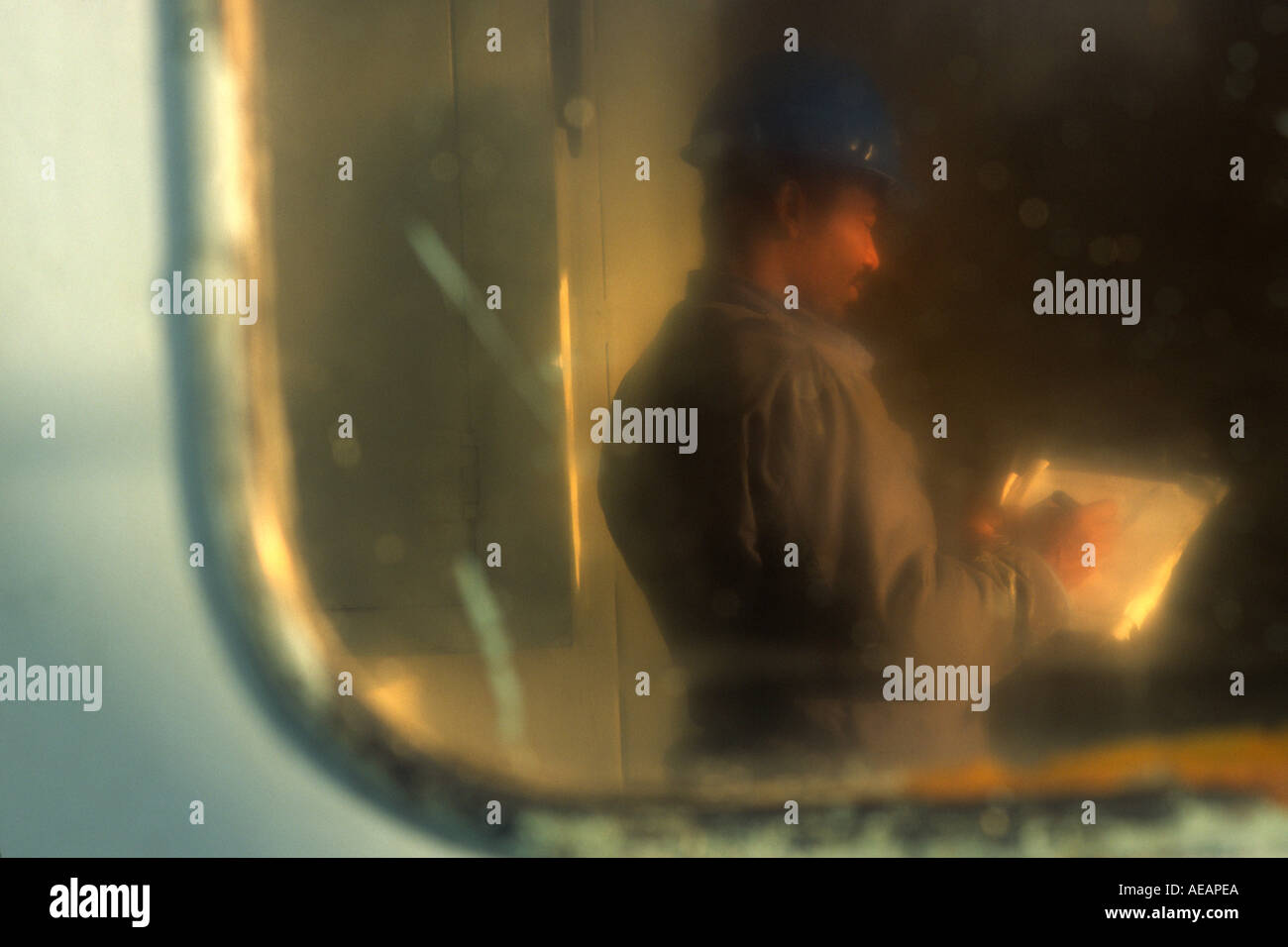 From ouside a window on an oil rig a man can be seen inside writing a ...