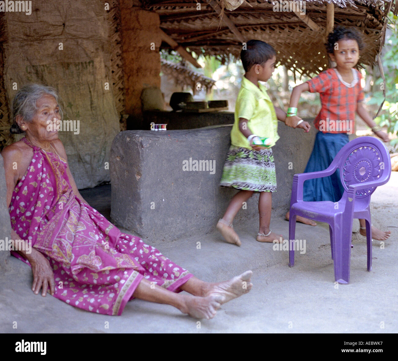 An old Indian tribal woman sits in front of her hut while her ...