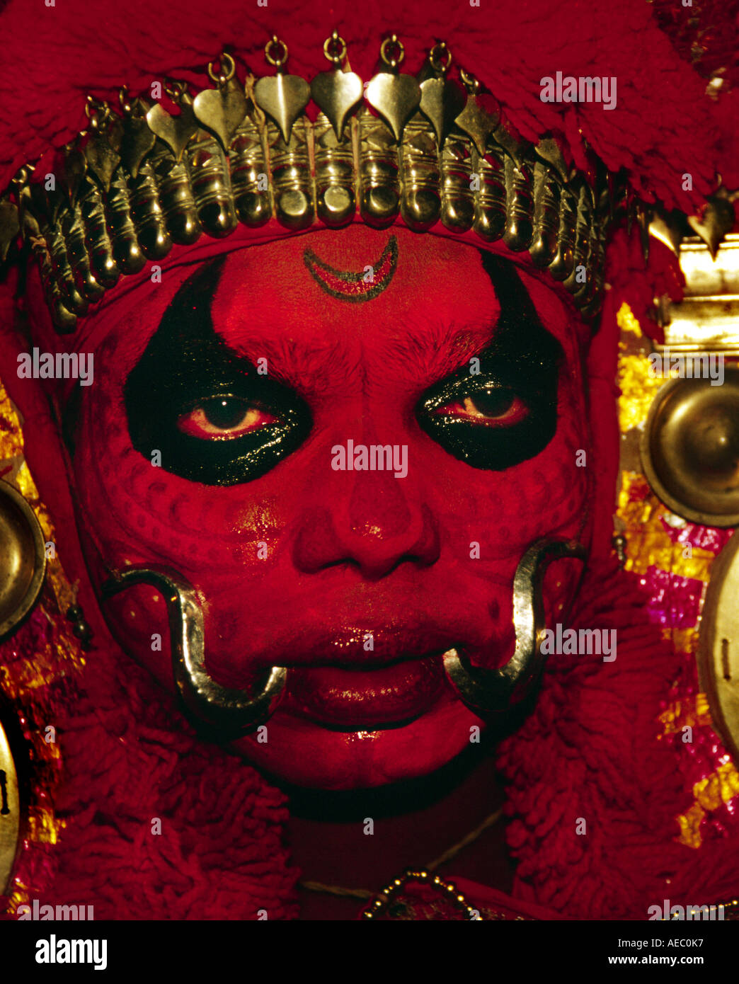 Close up of a Theyyam artist's face with traditional form of dark red ...
