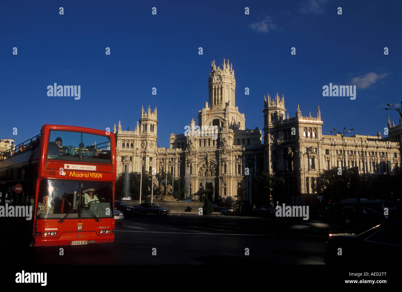 A Red Bus driving around Madrid with the Palace of Communications in ...