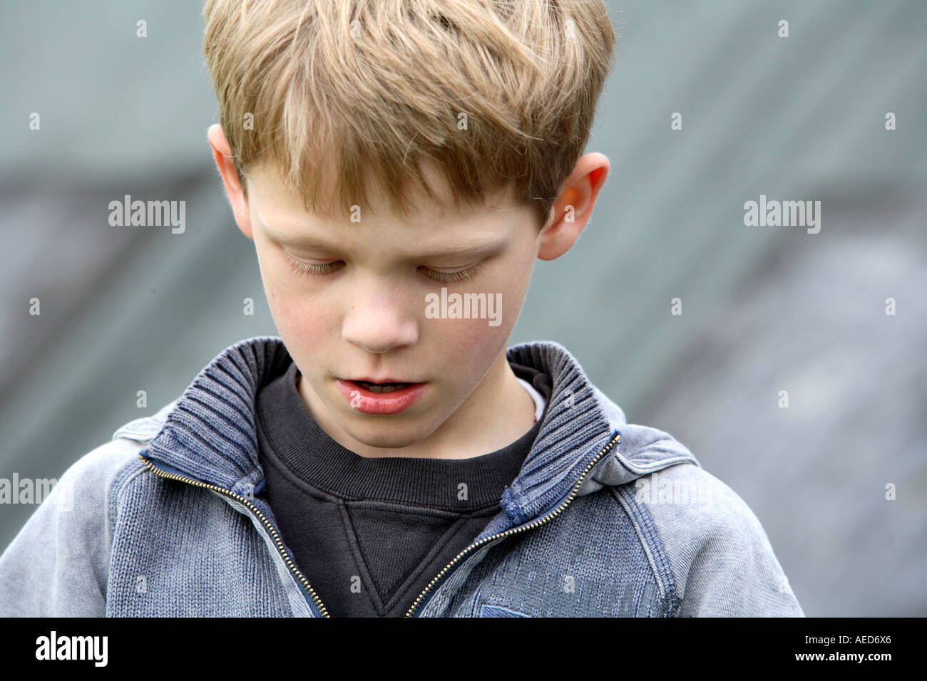 Horizontal close up portrait of blond young boy looking down at hands ...
