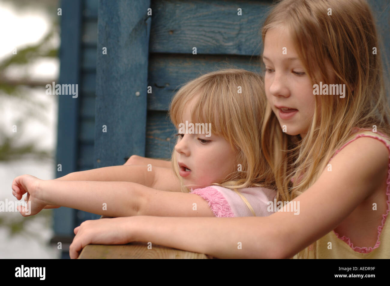 Two blond girls looking over handrail Stock Photo - Alamy