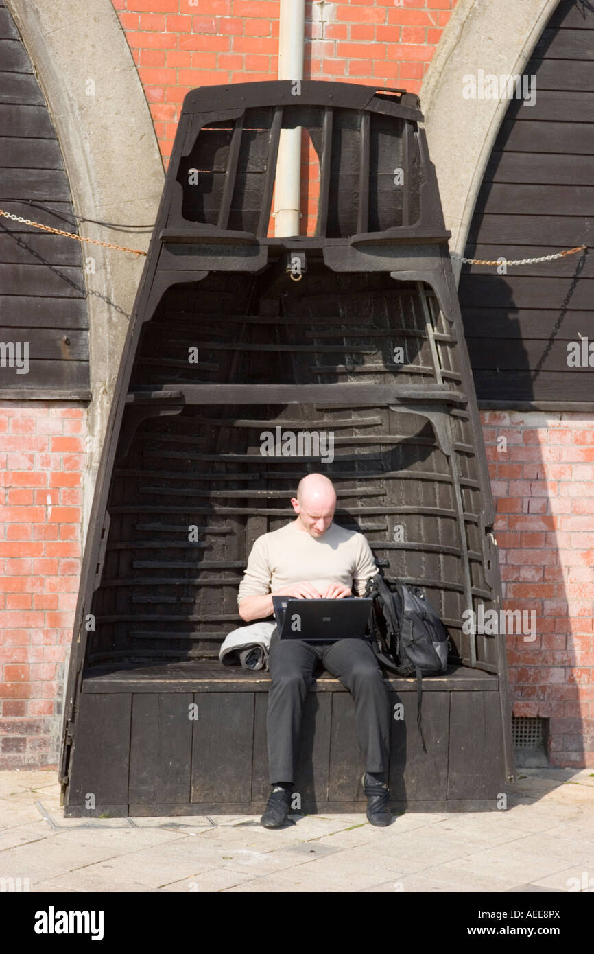 Man with laptop computer sitting in a seat made from an old wooden boat ...