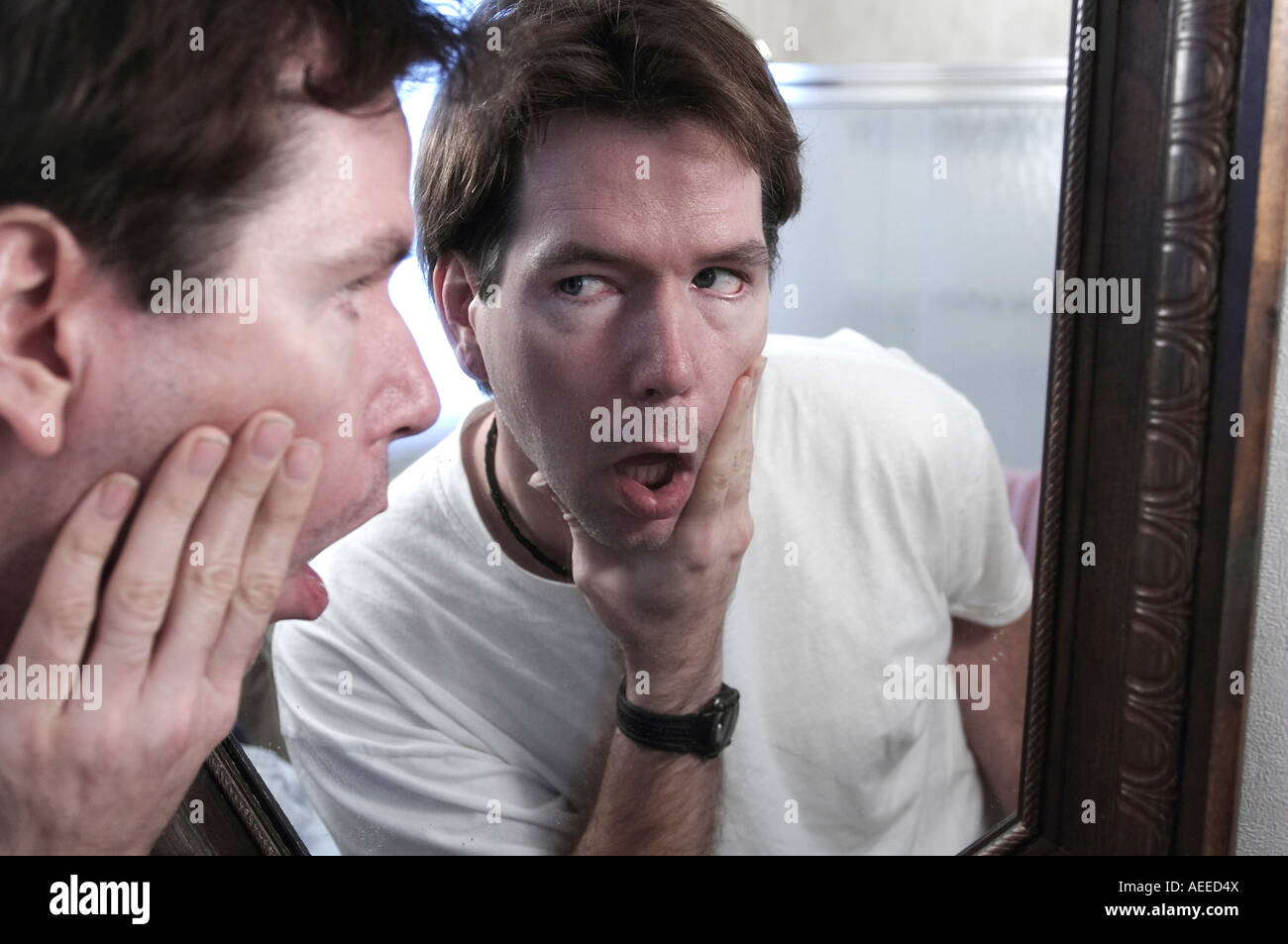A man pulling at his cheek while looking in the mirror in the morning ...