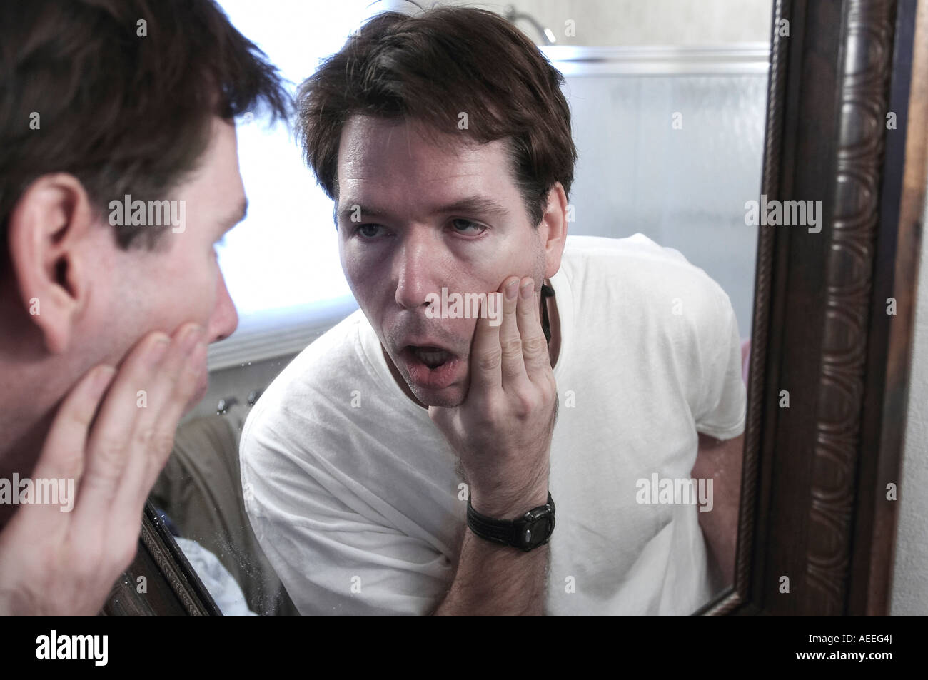 A man pulling at his face as he looks in the mirror in the morning ...