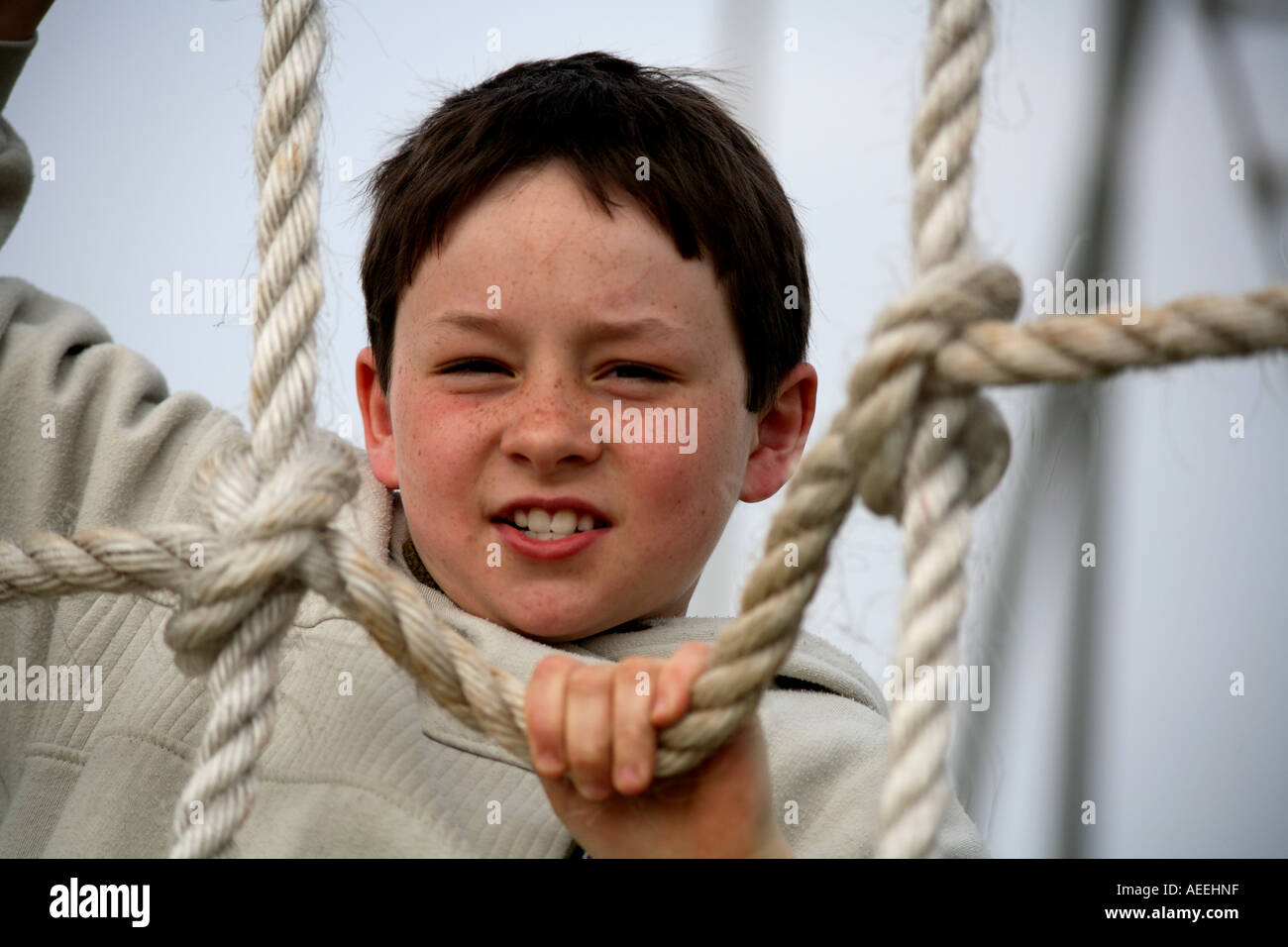 Horizontal close up portrait of young boy climbing rope ladder with ...