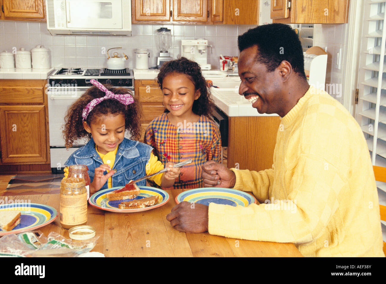 Dad and two daughters in kitchen making lunch fun multicultural multi ...