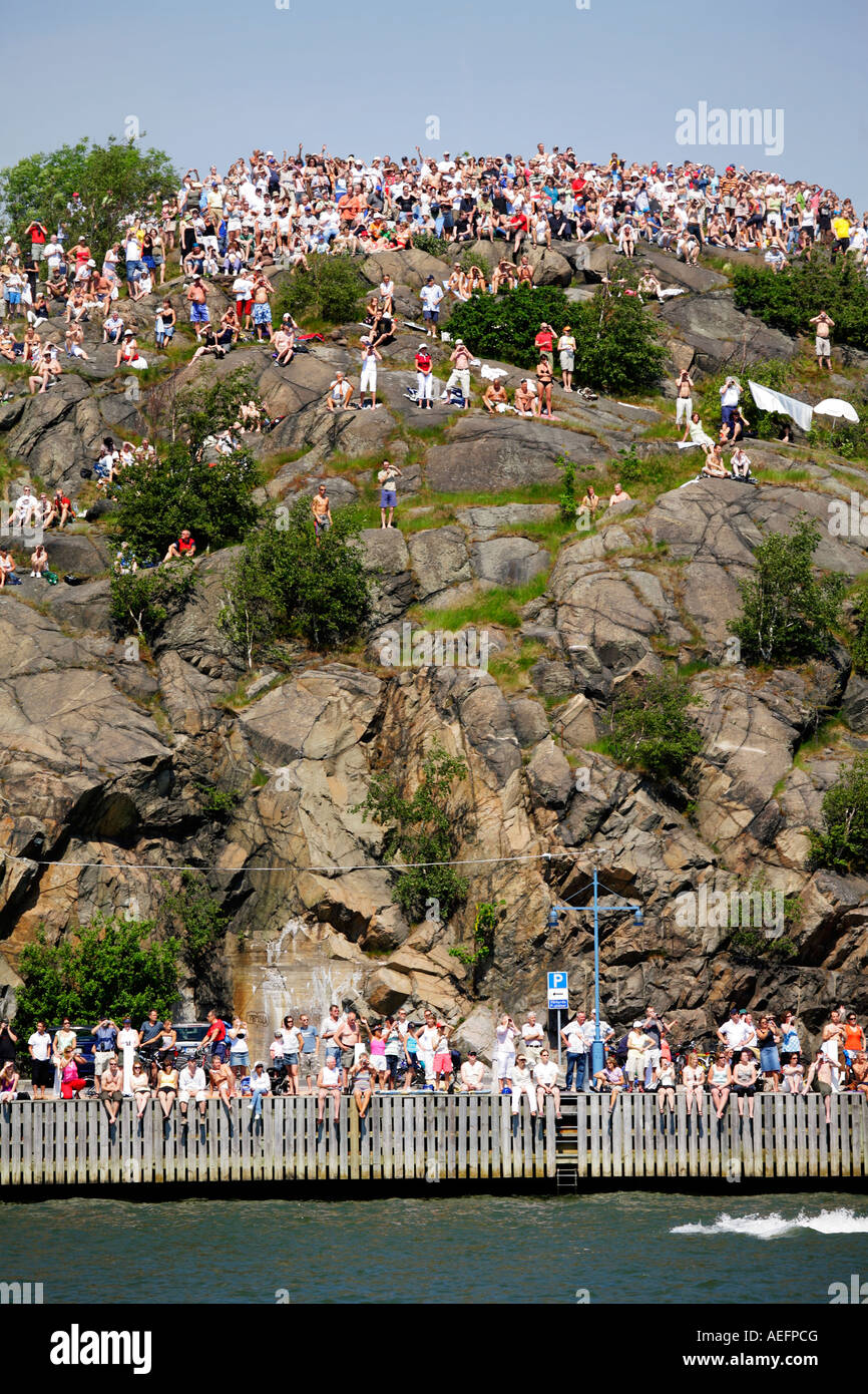 People crowding the rocky riverbank in an early sunny summer day ...