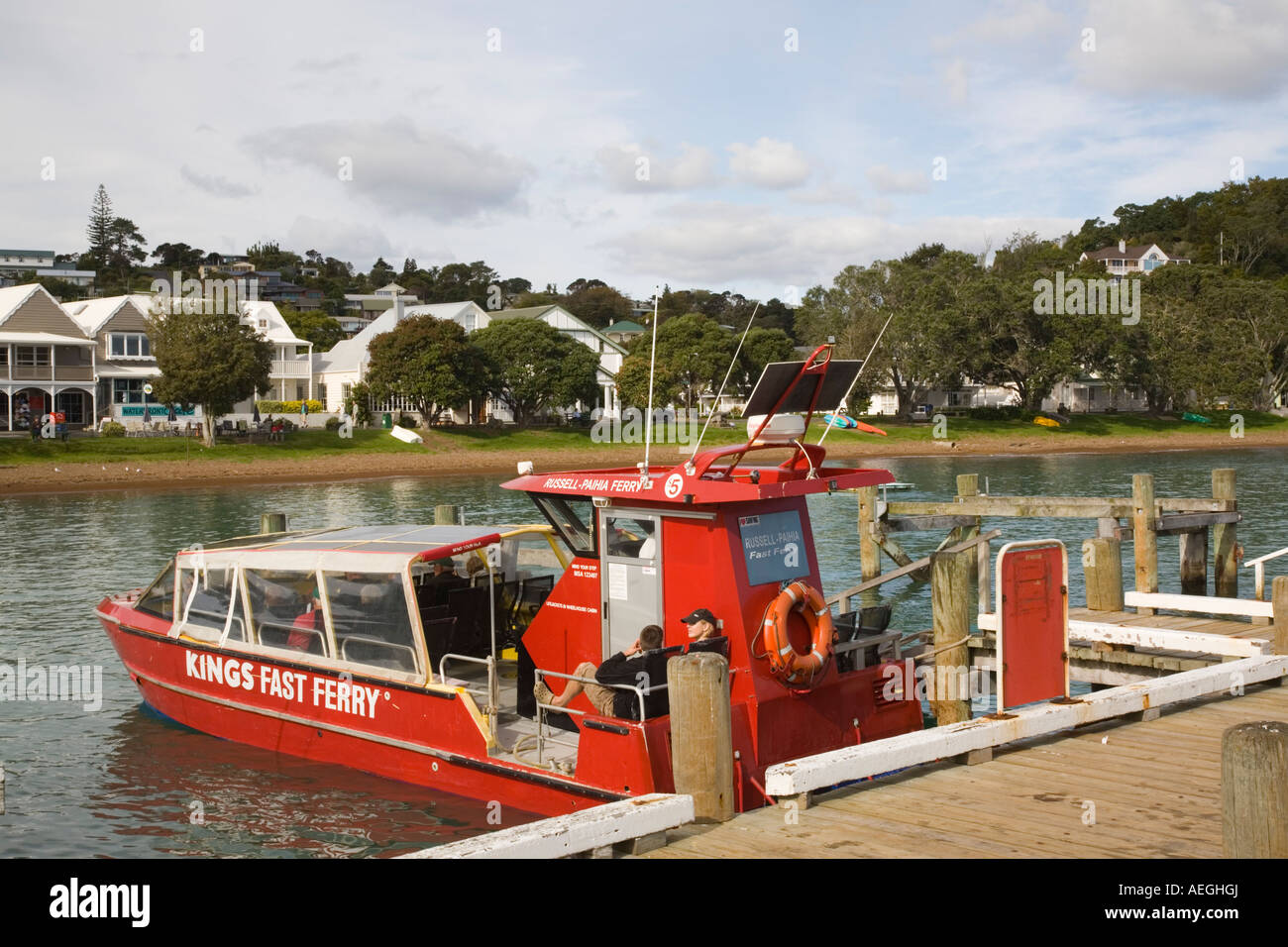 Fast red passenger ferry boat by wharf view across water to village ...