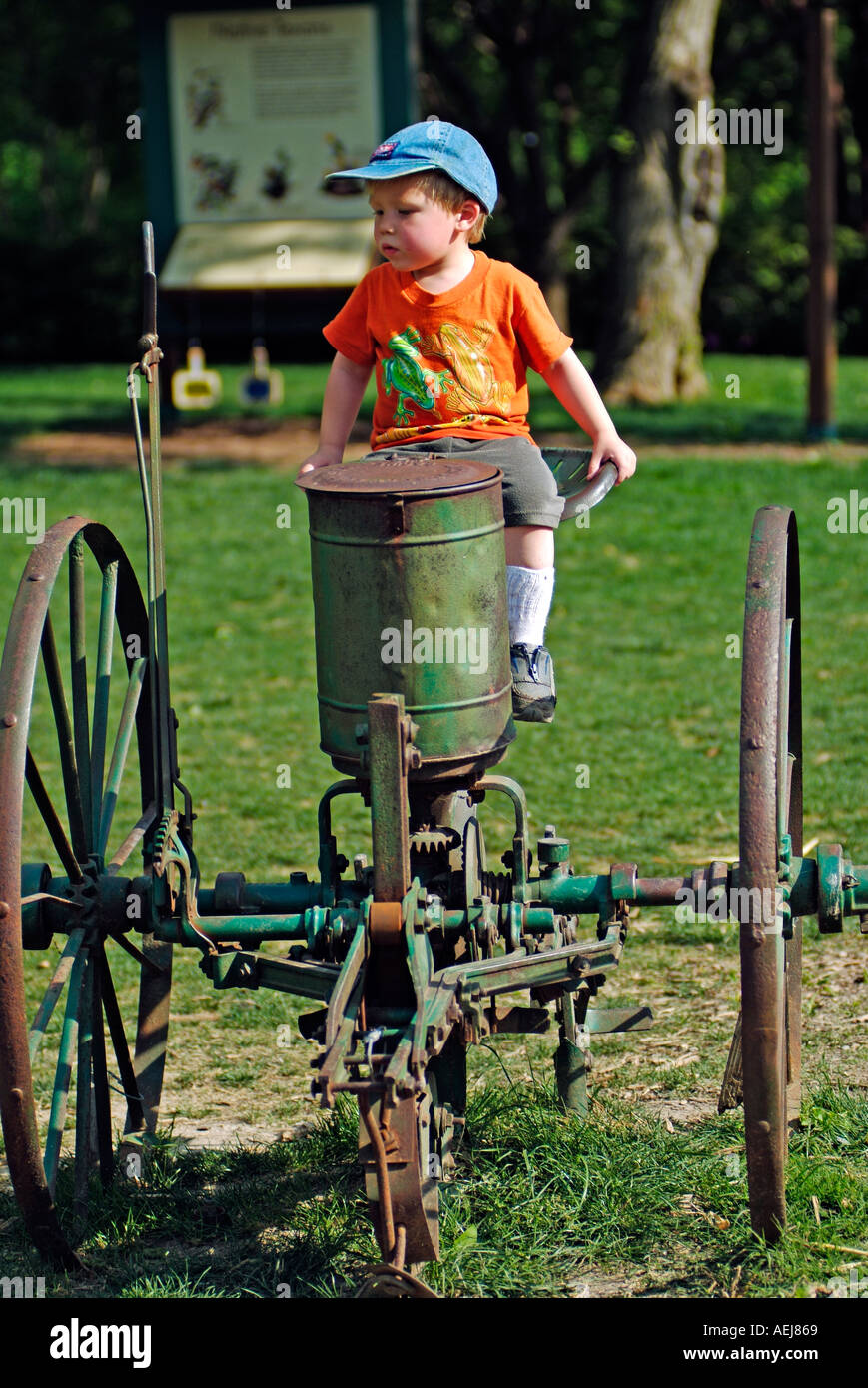 Young boy sitting on an old metal plow Stock Photo - Alamy