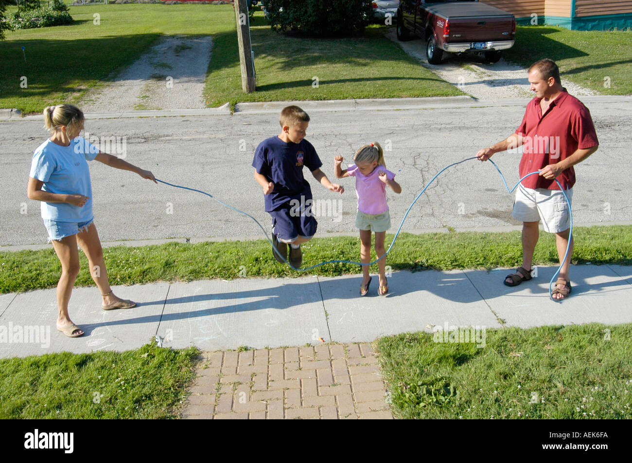 Family of four 4 play together jumping rope Stock Photo - Alamy