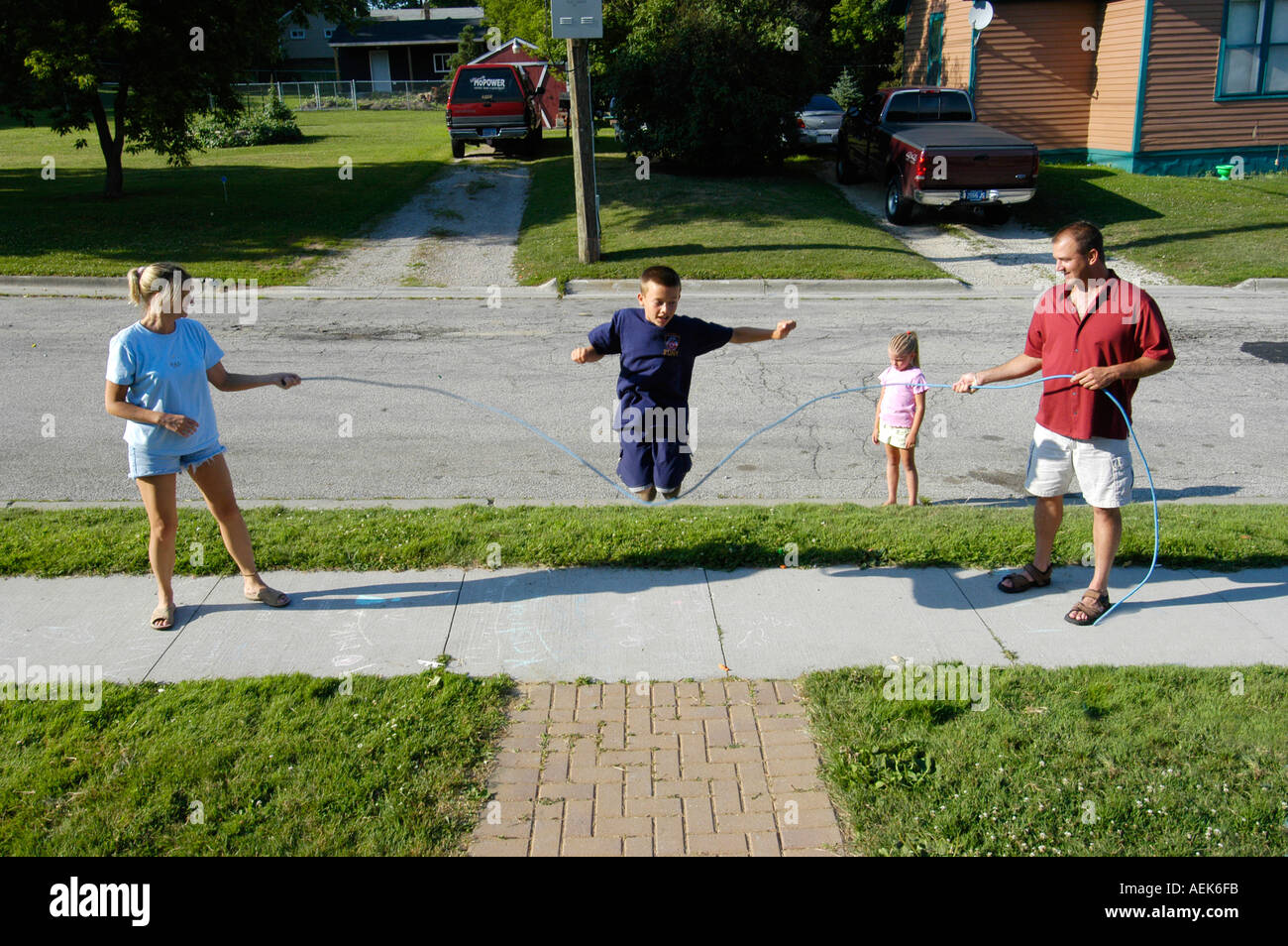 Family of four 4 play together jumping rope Stock Photo - Alamy