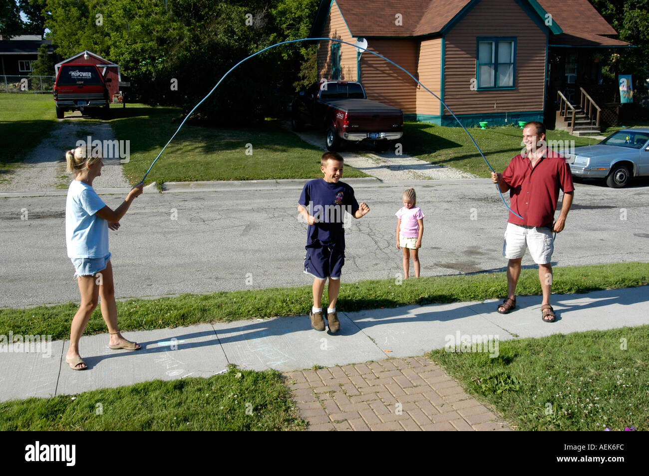 Family of four 4 play together jumping rope Stock Photo - Alamy