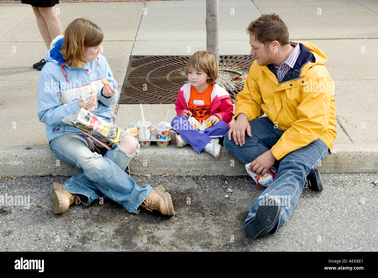 Family of 3 three eat lunch on a curb while attending a public event ...