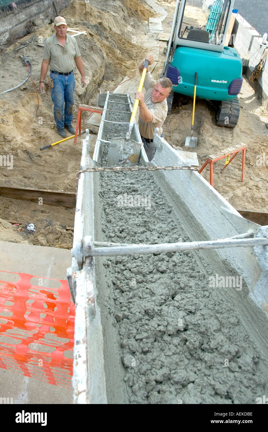 Foundation workers pull wet cement from truck to form footing for the ...