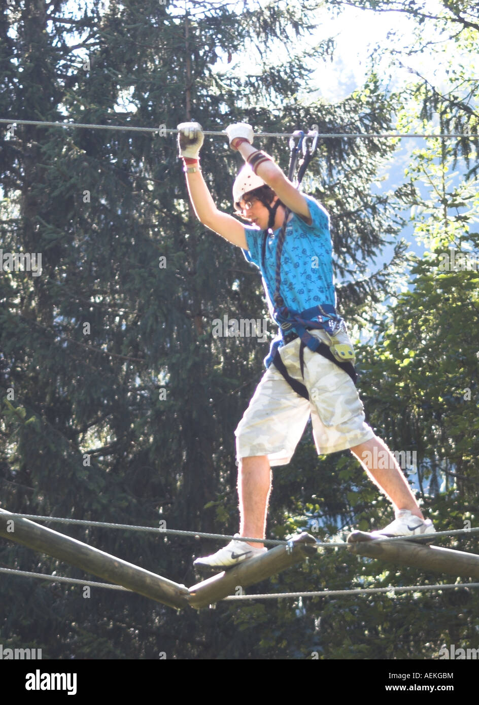 A young man crosses a rope bridge keeping his hands on the guide wire ...