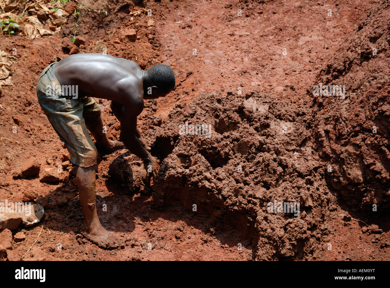 Young balck African man mixing the clay to make bricks in Western Kenya ...