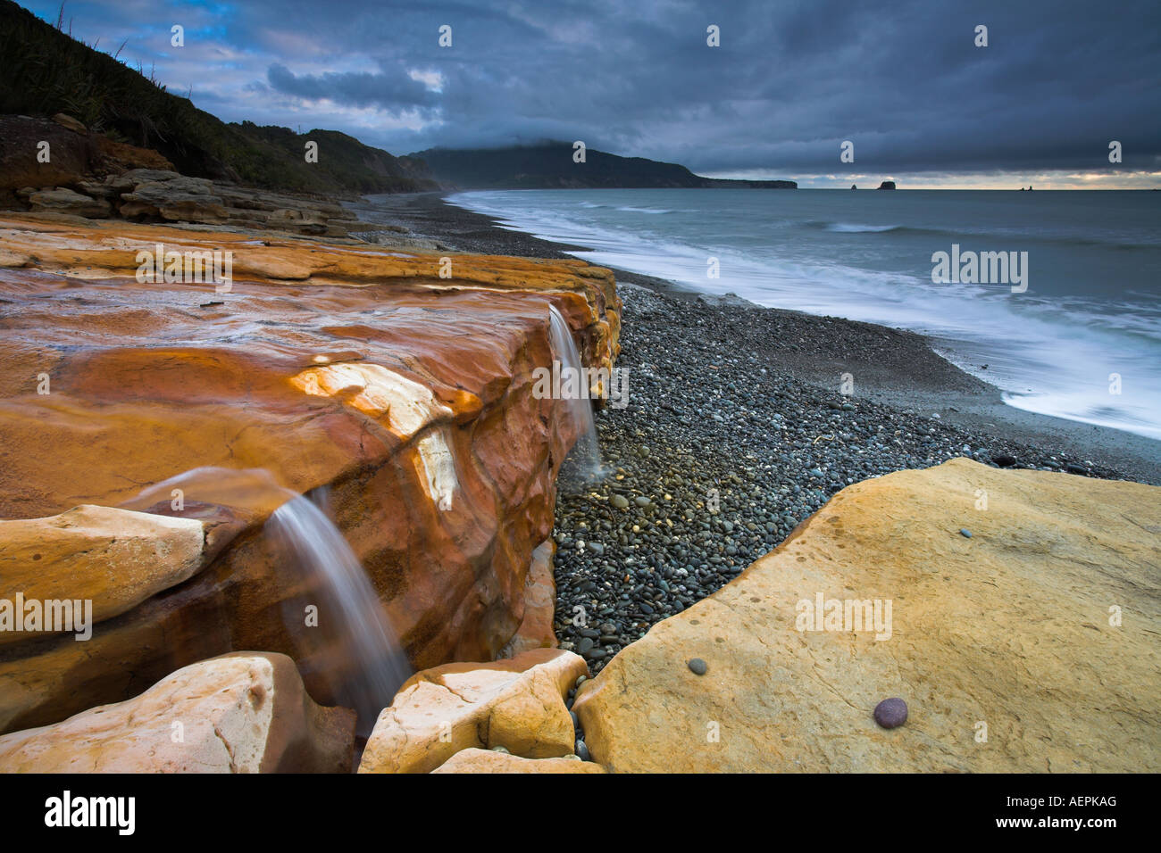 Waterfalls cascade over red sandstone on Seven Mile Beach, New Zealand ...