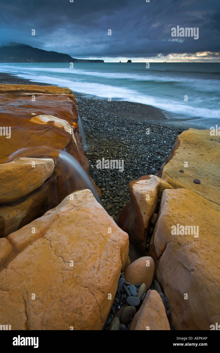 Waterfalls cascade over red sandstone on Seven Mile Beach, New Zealand ...