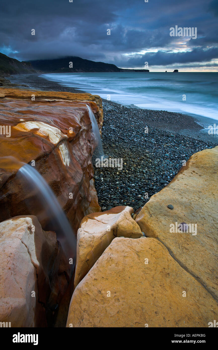 Waterfalls cascade over red sandstone on Seven Mile Beach, New Zealand ...