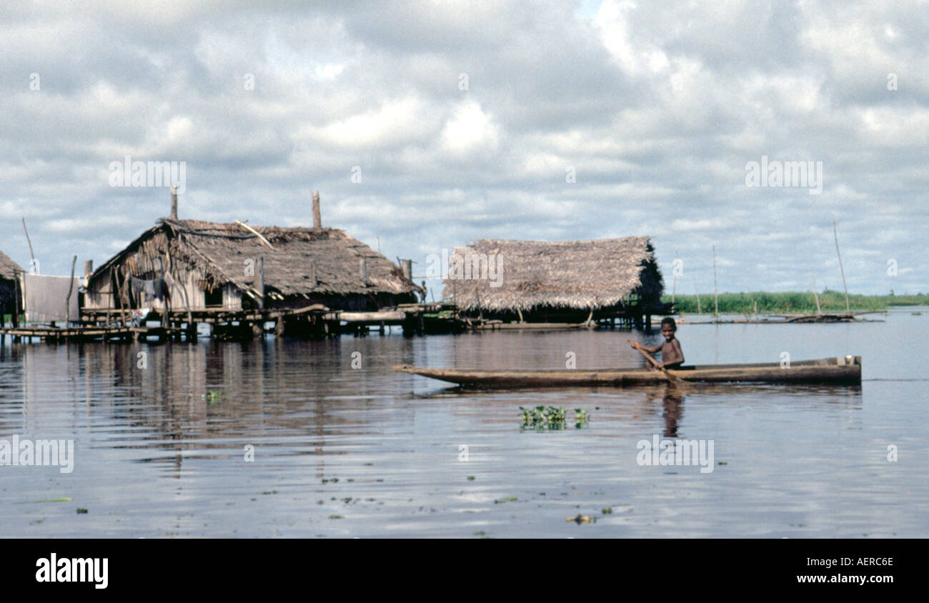 Boy in a canoe passes by houses on the flooded Sepik River Papua New ...