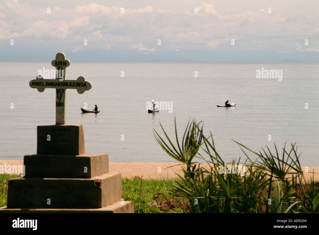 Usisya village grave stone by the lake with fishermen in dug out canoes ...