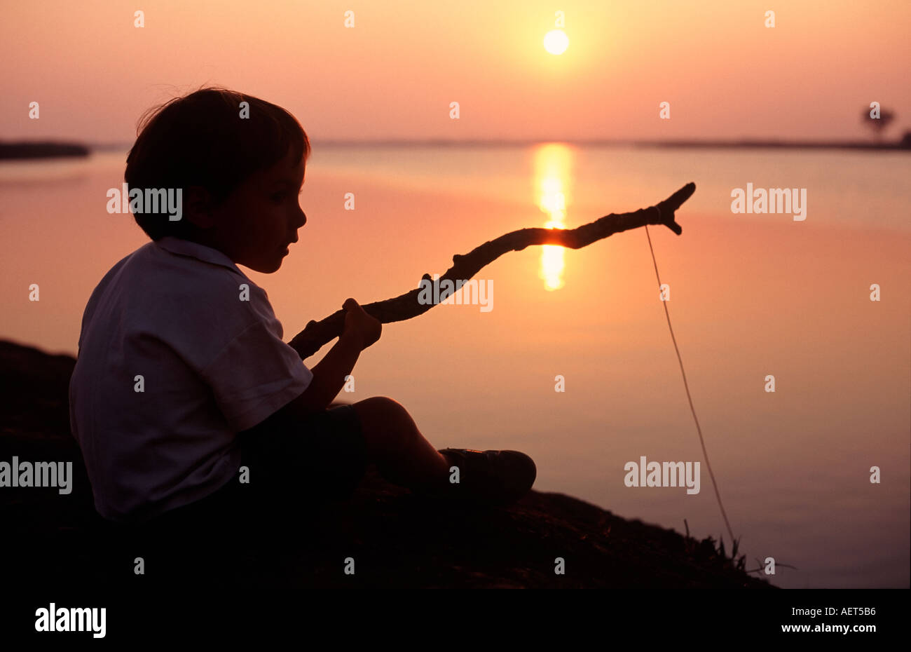 Young Boy Fishing with Wooden Stick at Sunset Stock Photo - Alamy