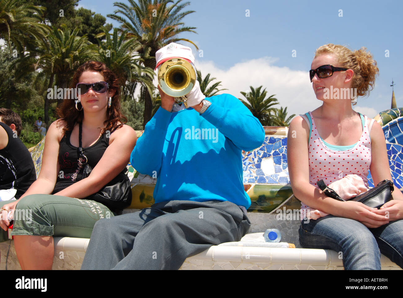 two young women with busker sitting on park bench in Parc Guell Barcelona Stock Photo - Alamy