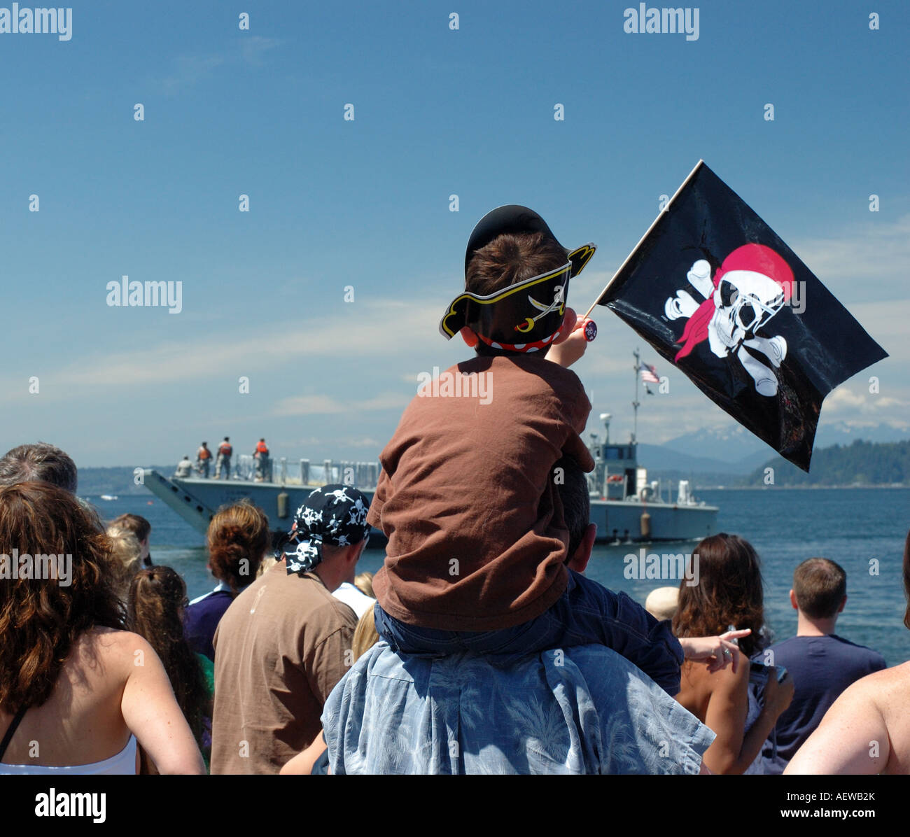 Boy sits on his father's shoulders and waves a pirate flag as boat ...