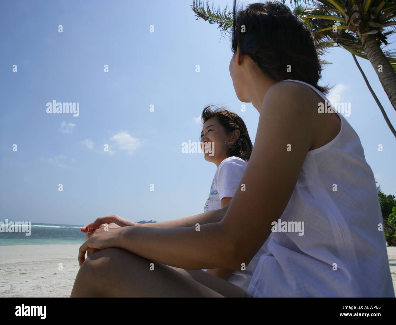 Side profile of two young women sitting on the beach Stock Photo - Alamy