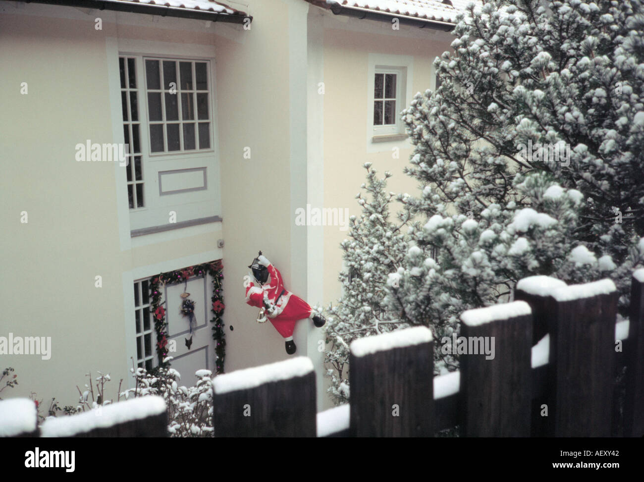 View over a fence on a house where Santa Claus is hanging at a lamp in ...