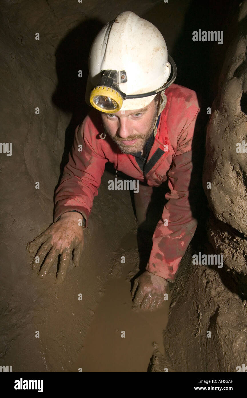 a male caver crawls through a tight constricted muddy passageway in the ...