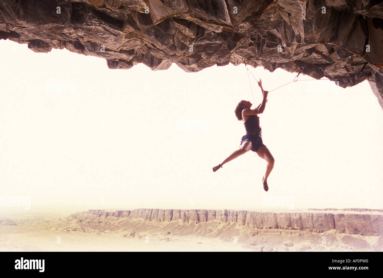 A woman climber hangs in her harness beneath a rock overhang in the ...
