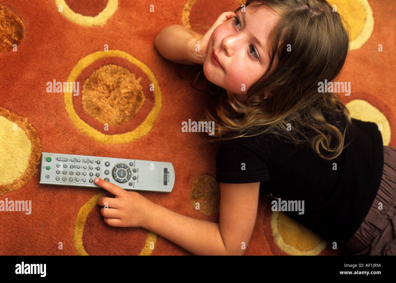 Young girl changing channels on a TV using a remote control at home ...