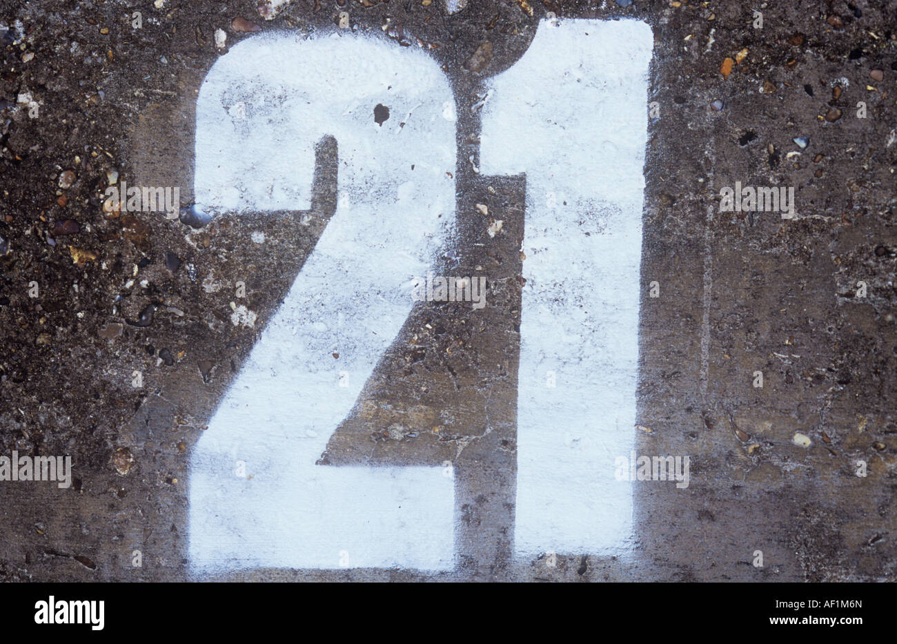 Close up of white painted stencilled number 21 on rough concrete wall ...