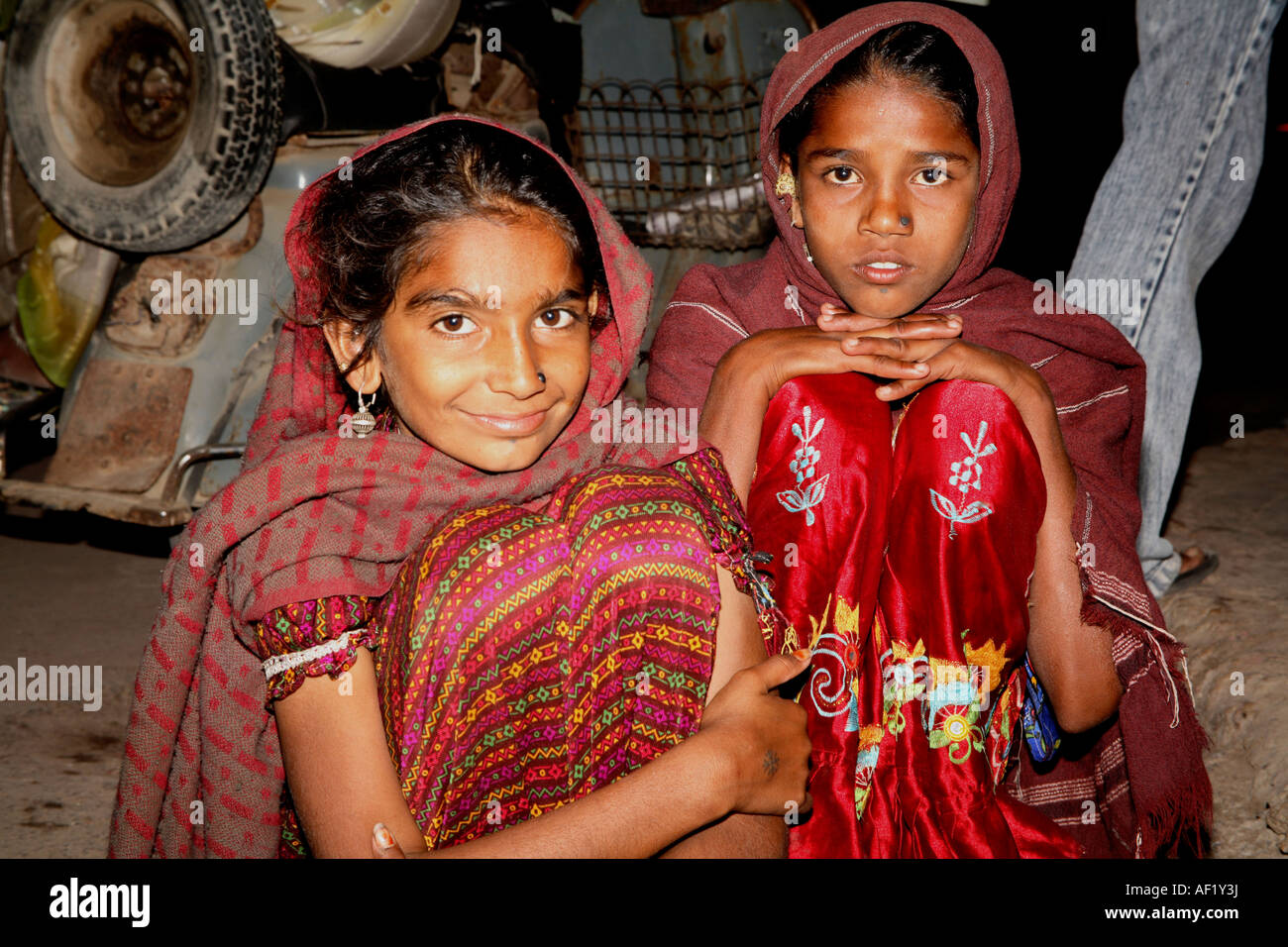 Portrait of two young Indian girls crouching on ground in High Street ...