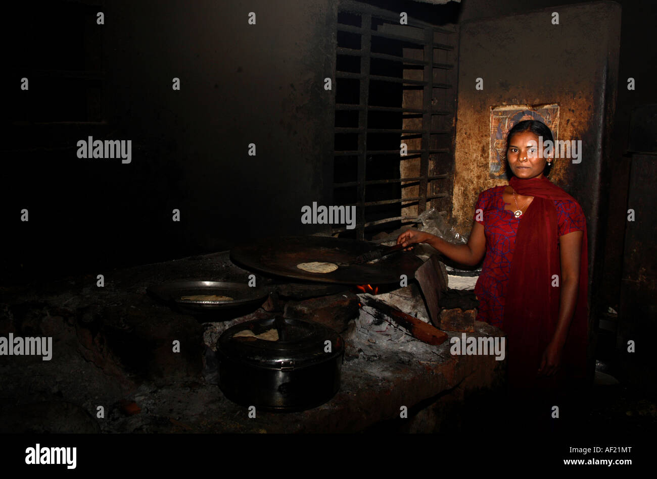 Young Indian female heating chapati on prehistoric stove in restaurant ...