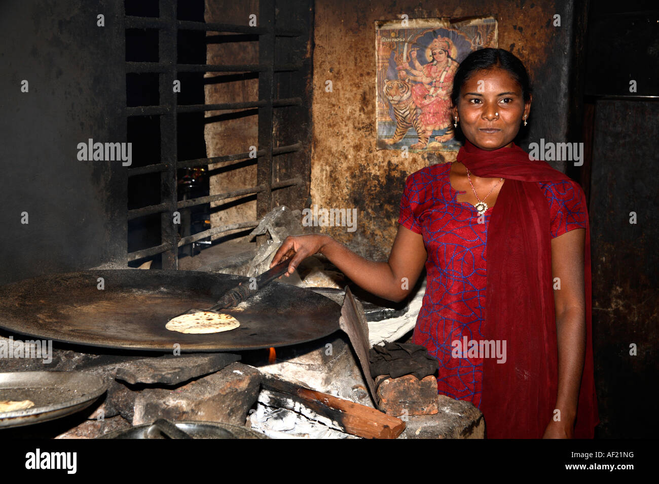 Young Indian female making chapati on prehistoric stove in restaurant ...