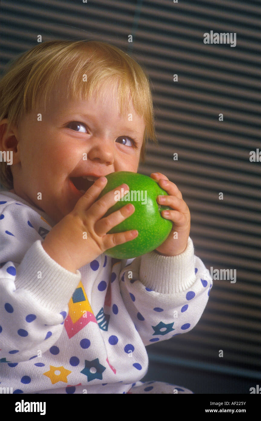 One year old girl eating green apple Stock Photo - Alamy