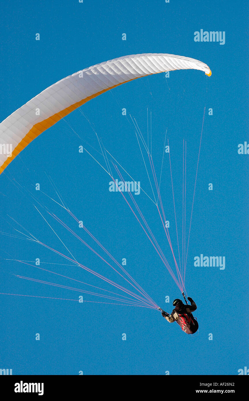 Pilot flying white and yellow paraglider against a perfectly blue sky ...