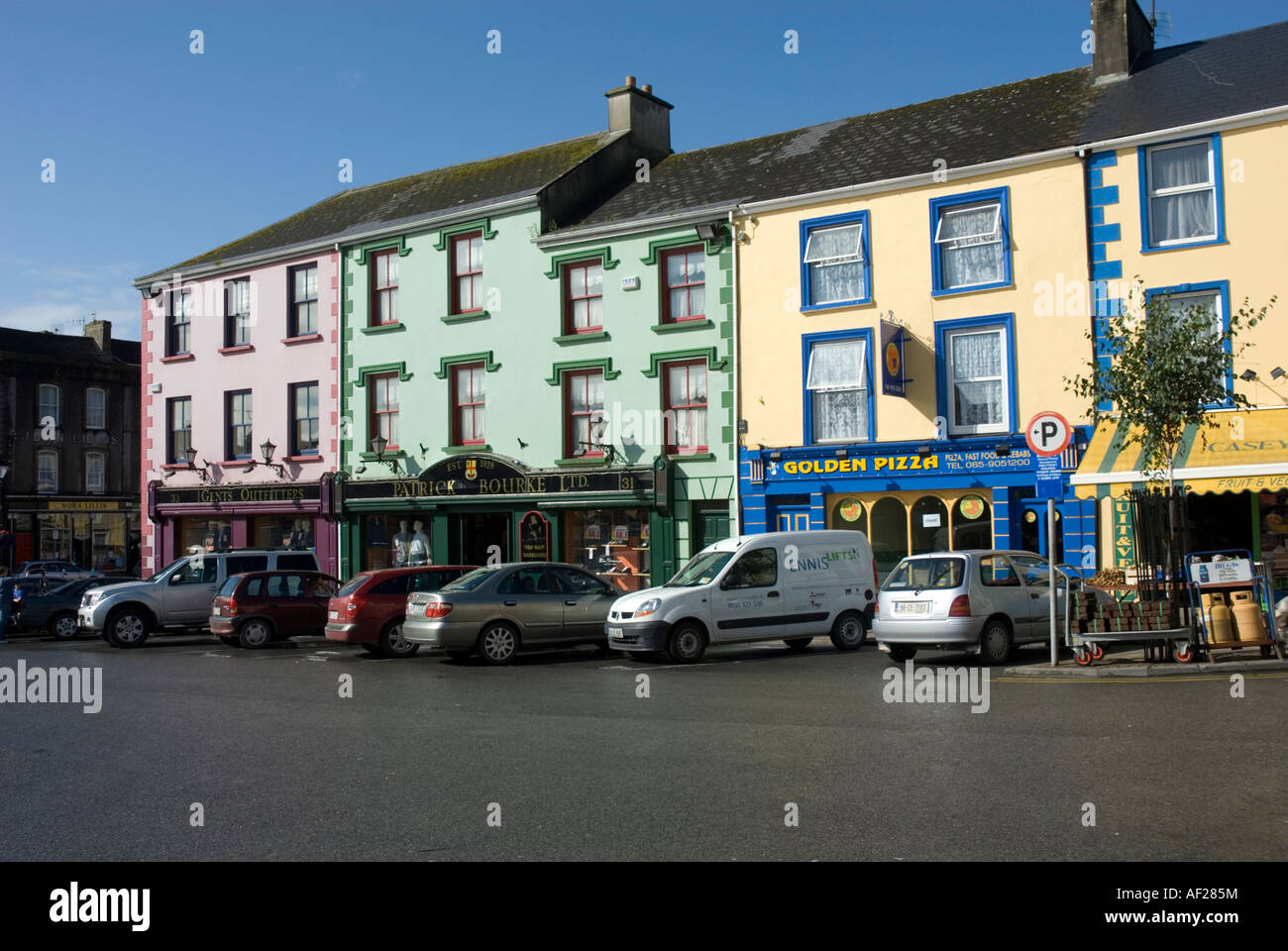colourful row of shops in morning sunlight with cars parked outside ...