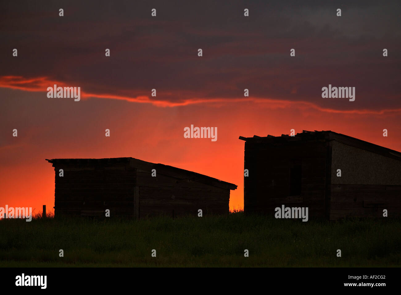 Setting sun lighting up clouds behind two farm buildings in scenic ...