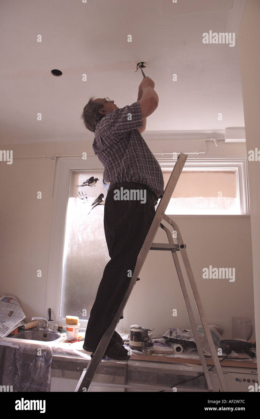 Overweight Older man up ladder putting in lighting fixture in his ...