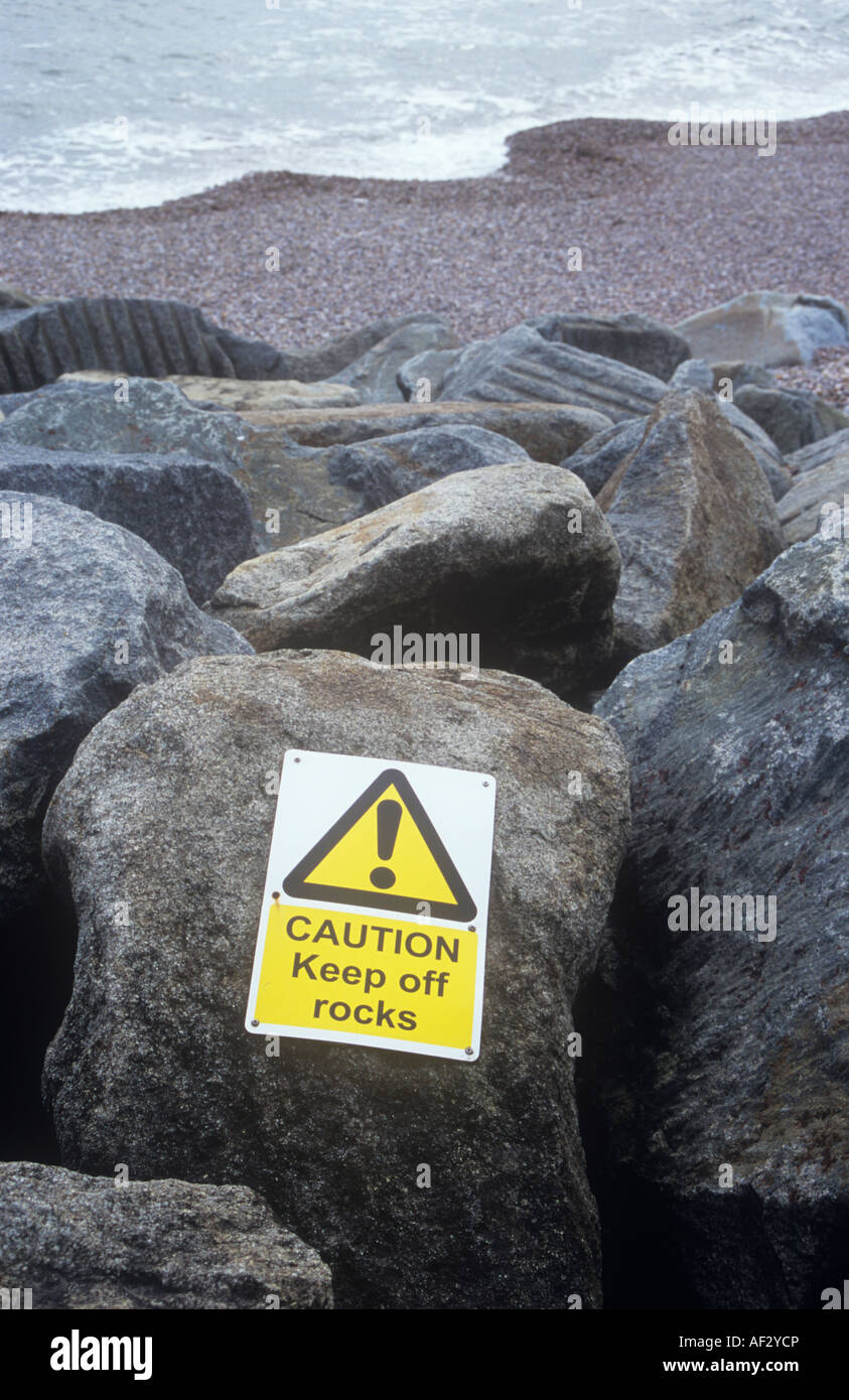 Sea defence rocks with pink shingle beach and grey sea beyond with sign ...