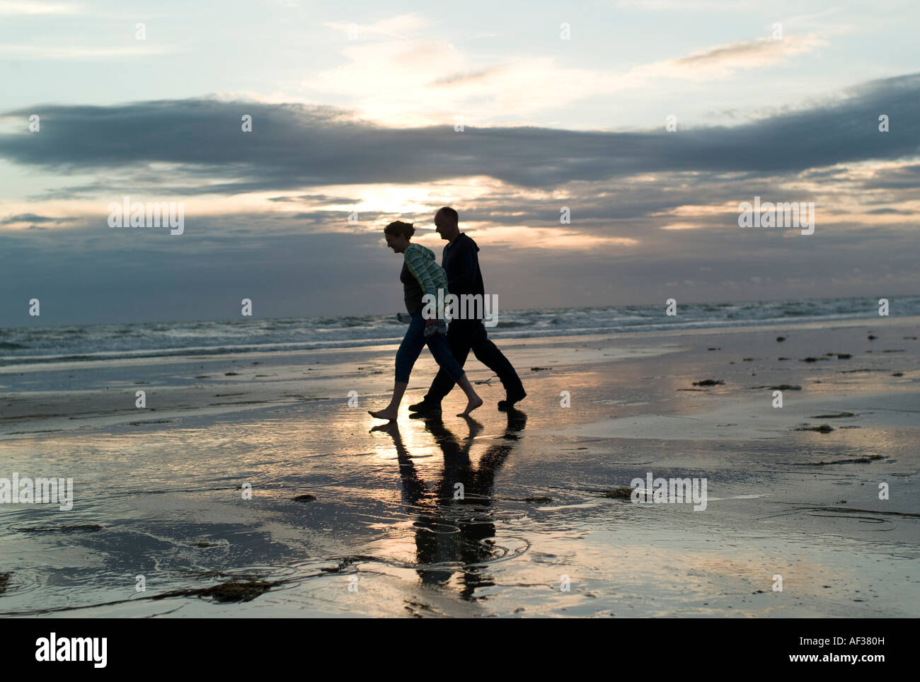 Two people - man and woman - walking on Borth beach west wales at ...