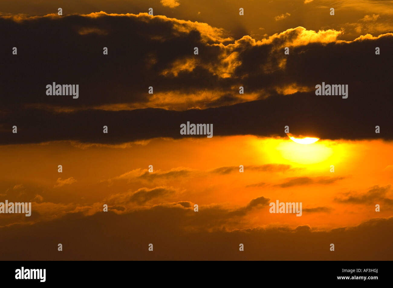 The sun dropping down from under cloud cover giving a red warm glow to ...