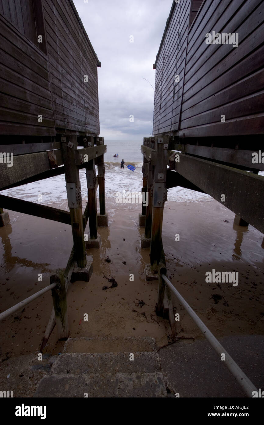 Beach huts and stairs leading to Frinton beach and swimmers in sea ...