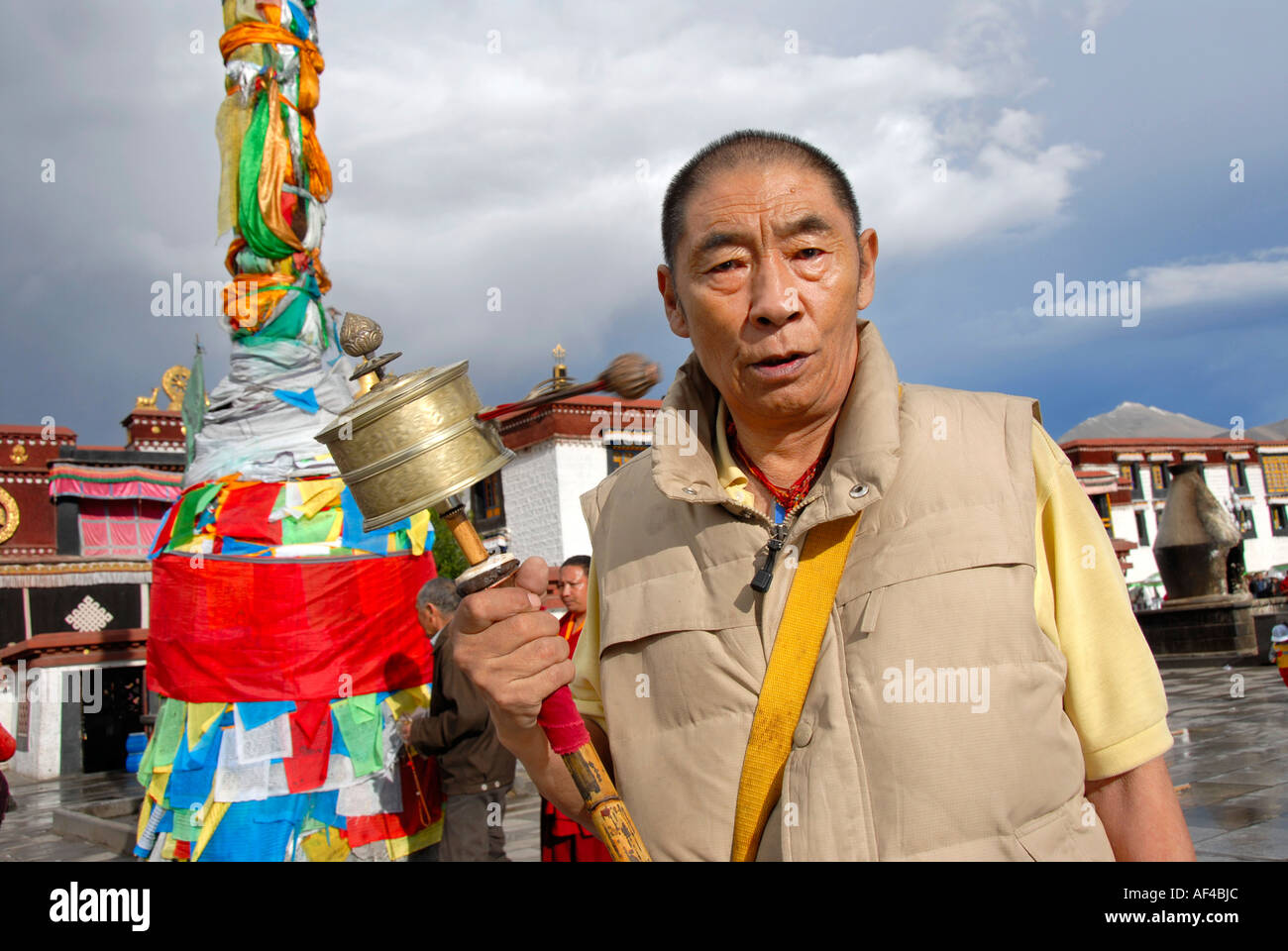 Tibetan pilgrim with prayer wheel at the Kora with colourful prayer ...